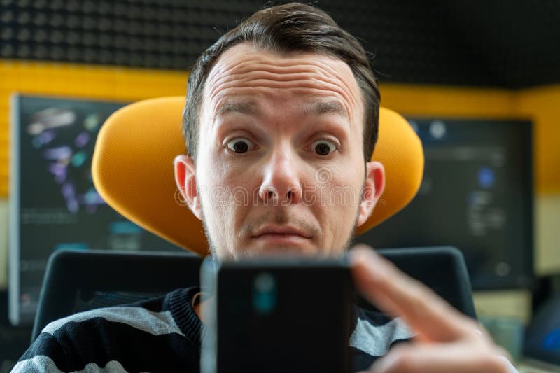 Surprised Man Looking at Smartphone in Tech Workspace, Indicating ...