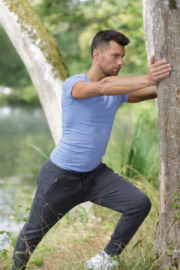Young Man Doing Stretching Against Tree In Park Stock Image - Image of ...
