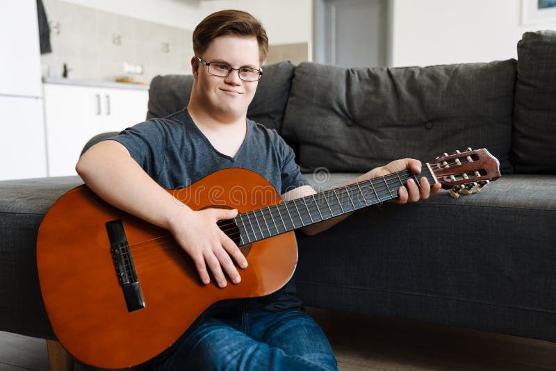 Young Man with Down Syndrome Playing Guitar while Sitting on Floor ...