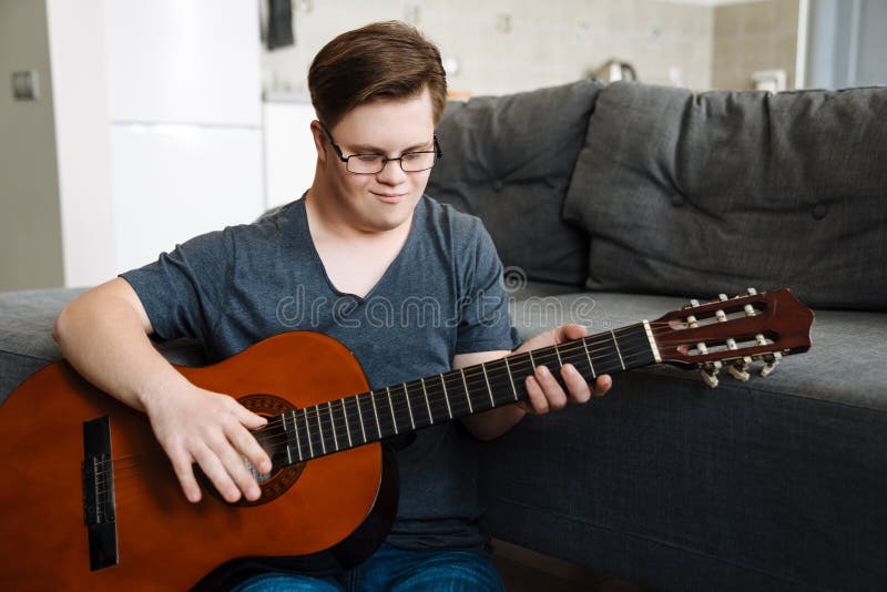 Young Man with Down Syndrome Playing Guitar while Sitting on Floor ...