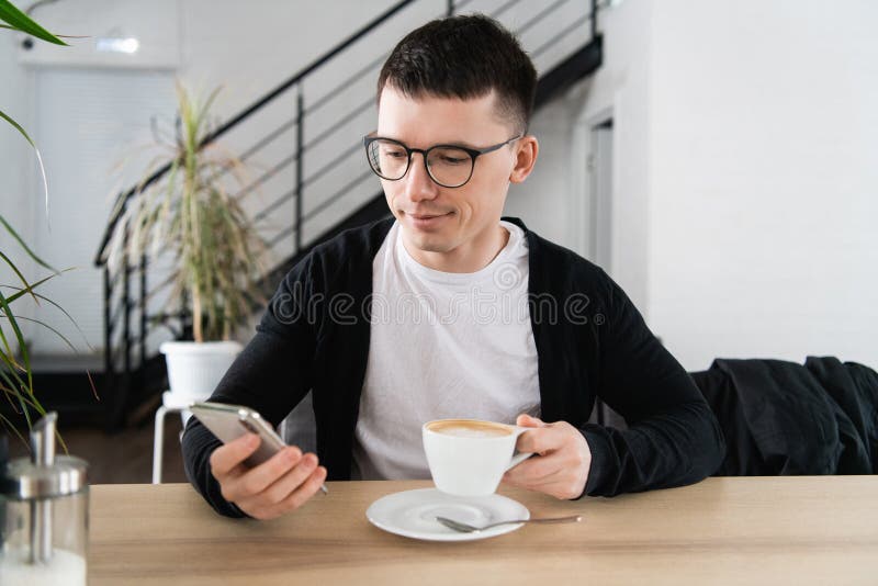 Young Man Drinking Coffee in Cafe and Using Phone Stock Photo - Image ...
