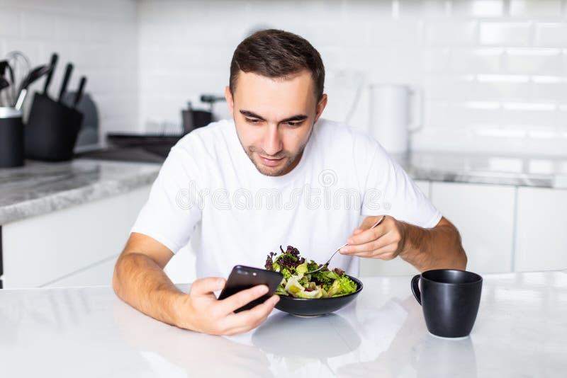 Young Man Eating Breakfast Using Mobile Phone in the Kitchen Stock ...