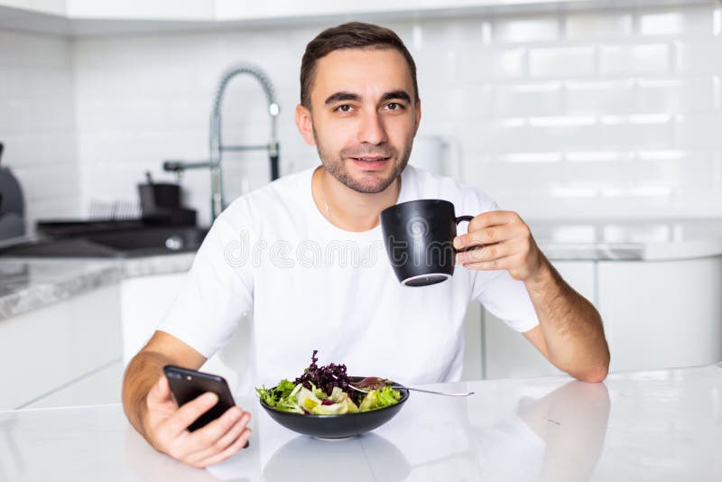 Young Man Eating Breakfast Using Mobile Phone in the Kitchen Stock ...