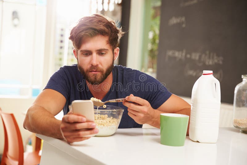 Young Man Eating Breakfast Whilst Using Mobile Phone Stock Photo ...