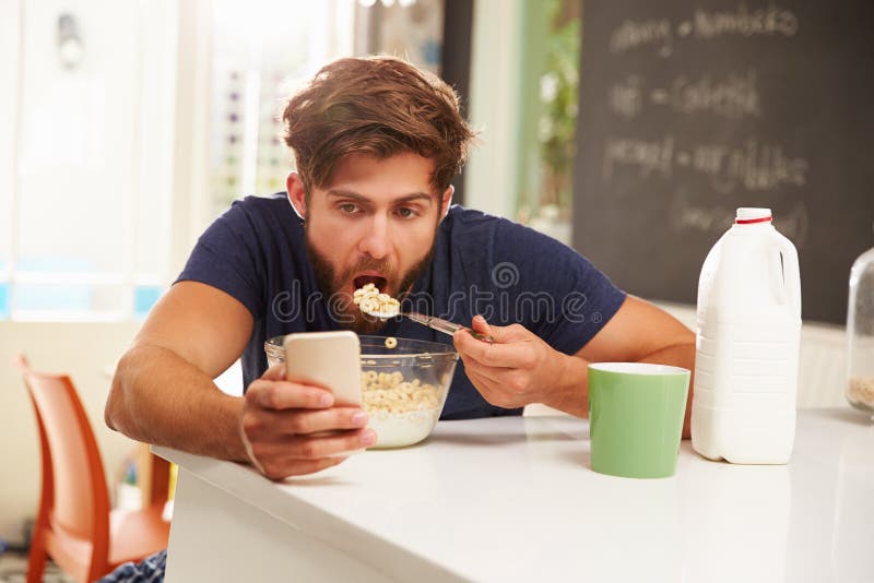 Young Man Eating Breakfast Whilst Using Mobile Phone Stock Image ...