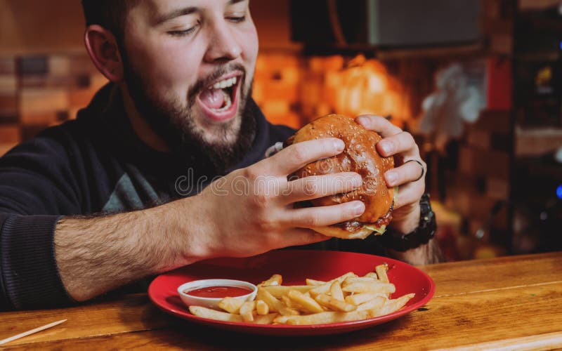 Young Man Eating a Cheeseburger. Restaurant Background. Stock Photo ...