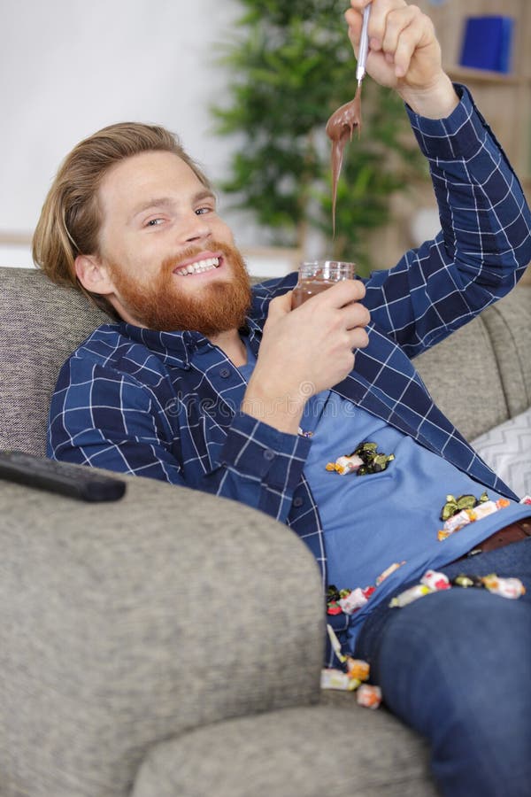 Young Man Eating Chocolate while Sitting on Sofa at Home Stock Image ...