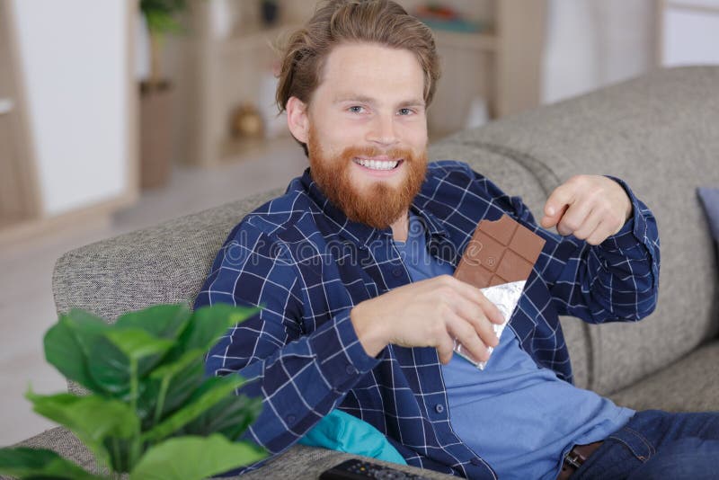 Young Man Eating Chocolate on Sofa Stock Photo - Image of eating, male ...