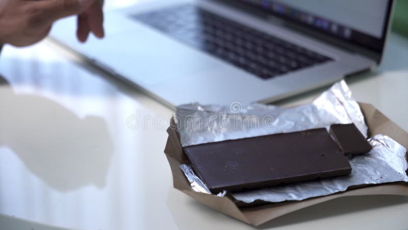 Young Man Eating Chocolate while Working with Laptop in Office. Close ...