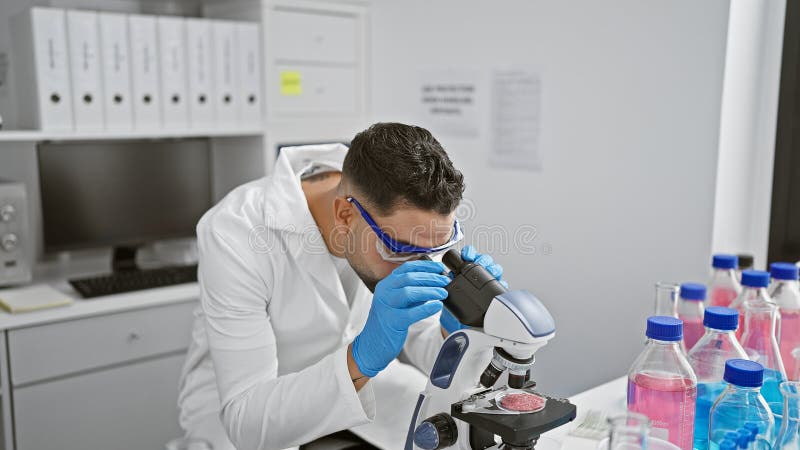 A Young Man Examines Specimens Under a Microscope in a Laboratory ...