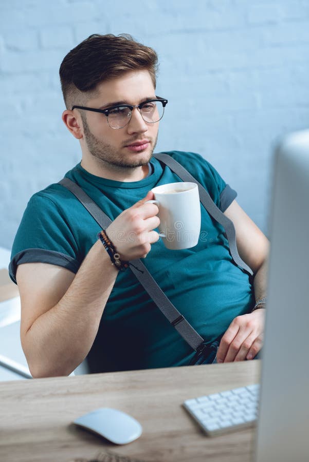 Young Man in Eyeglasses Drinking Coffee and Working with Desktop ...