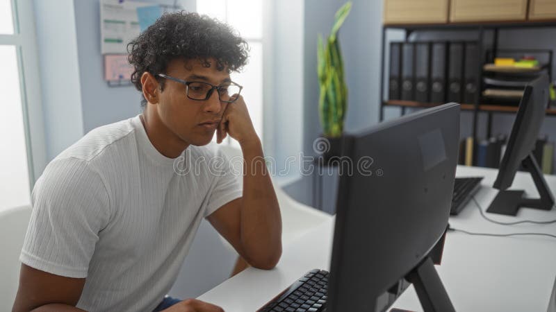 Young Man Focused on Computer Work in a Bright, Modern Office Adorned ...
