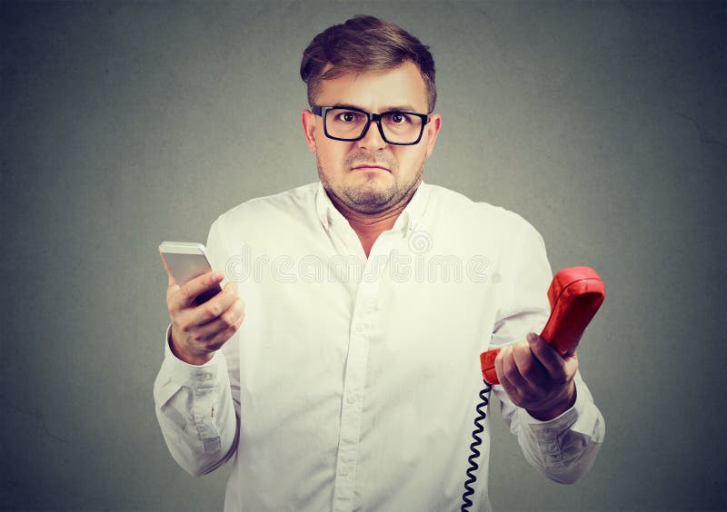 Confused Man Holding Old Fashioned Red Phone And Modern Smarpthone