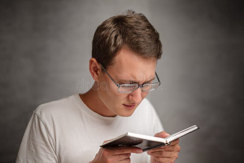 The Young Man Holds Glasses with Diopter Lenses and Looking at the Book ...