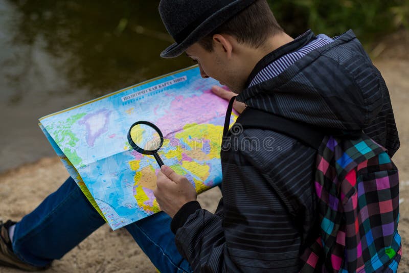 Young Man Holds a Map and Looks through a Magnifying Glass Stock Photo ...
