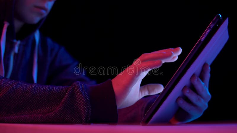 Young Man in a Hood with a Tablet. Hacker Makes a Hack through the ...