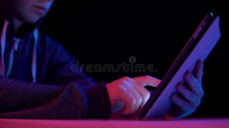 Young Man in a Hood with a Tablet. Hacker Makes a Hack through the ...