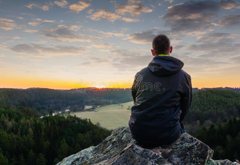 Young Man in Jacket, Pants and Sitting on Rock Looking To Valley at ...