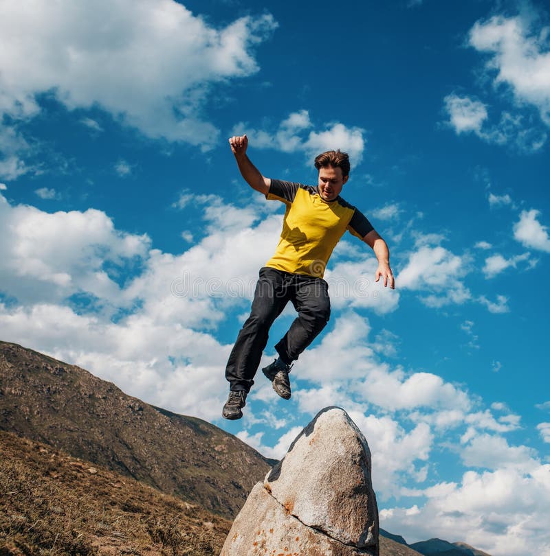 Man Jumping from Big Stone on Mountains Background Stock Image - Image ...