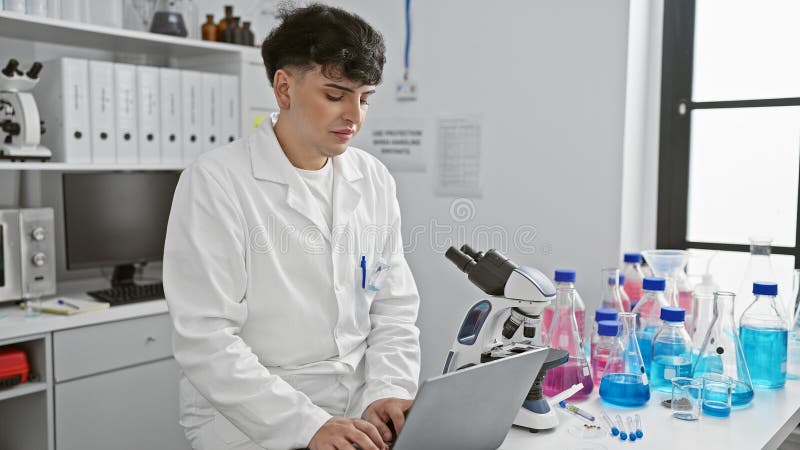 A Young Man in a Lab Coat Analyzing Data on a Laptop in a Modern ...