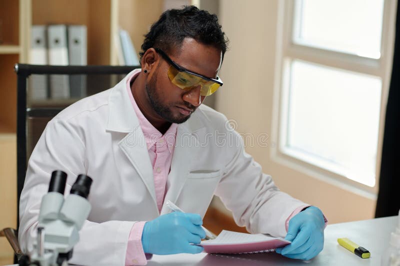Young Man in Lab Coat and Gloves Making Notes in Copybook Stock Photo ...