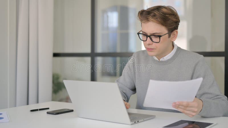 Young Man with Laptop Reading Documents in Modern Office Stock Image ...