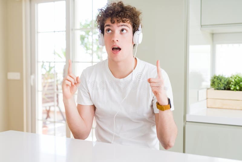 Young Man Listening To Music Wearing Headphones At Homes Amazed And