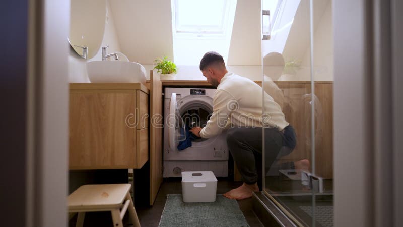 Young Man Loading Clothes into Washing Machine in Bathroom Stock ...