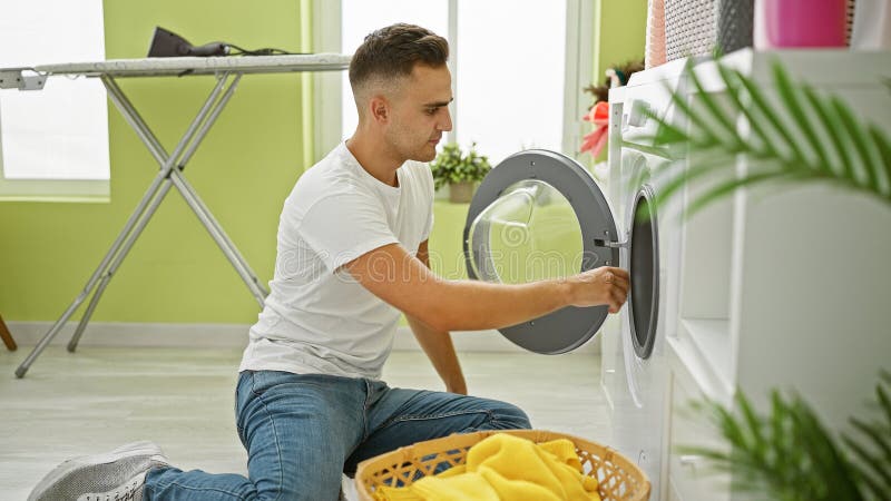A Young Man is Loading Laundry into a Washing Machine in a Bright Home ...