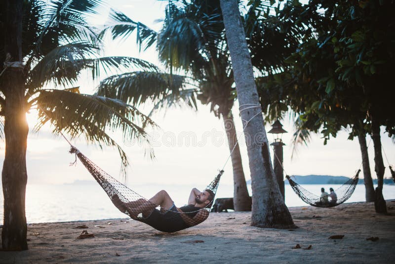 A Man is Lying in a Hammock at Sunset by the Ocean. Handsome Guy is ...