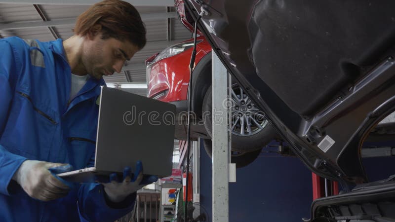 Young Man is Mechanic Using Laptop Computer Checking Engine of Car in ...