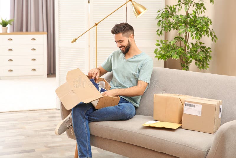 Young Man Opening Parcel with Shoes on Sofa Stock Photo - Image of ...