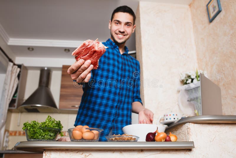 Young Man Preparing Meat in Her Kitchen , Looking into the Frame Stock ...