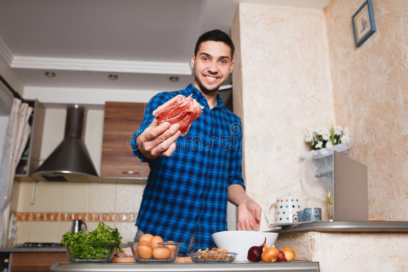 Young Man Preparing Meat in Her Kitchen , Looking into the Frame Stock ...