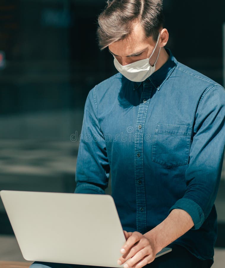 Young Man in a Protective Mask is Working on a Laptop, Sitting on a ...