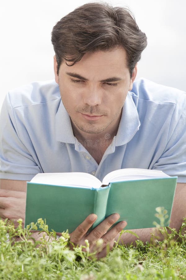 Young Man Reading Book on Grass Against Sky Stock Image - Image of ...