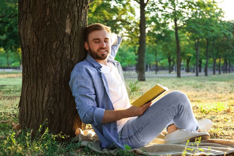 Young Man Reading Book on Green Grass Near Tree in Park Stock Image ...
