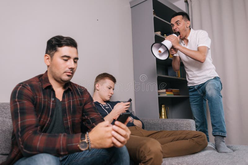 Three Cheerful Young Guys Are Sitting On Couch At Home And Have Fun ...