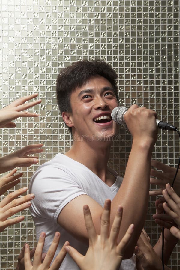 Young Man Singing into a Microphone with Lots of Hands Reaching for Him ...