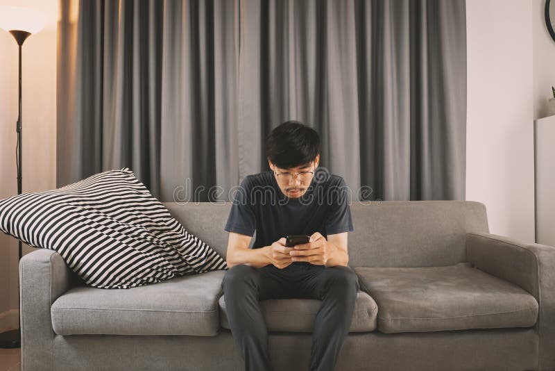 Young Man Sit Down on the Sofa while Using Mobile Phone and Drink ...