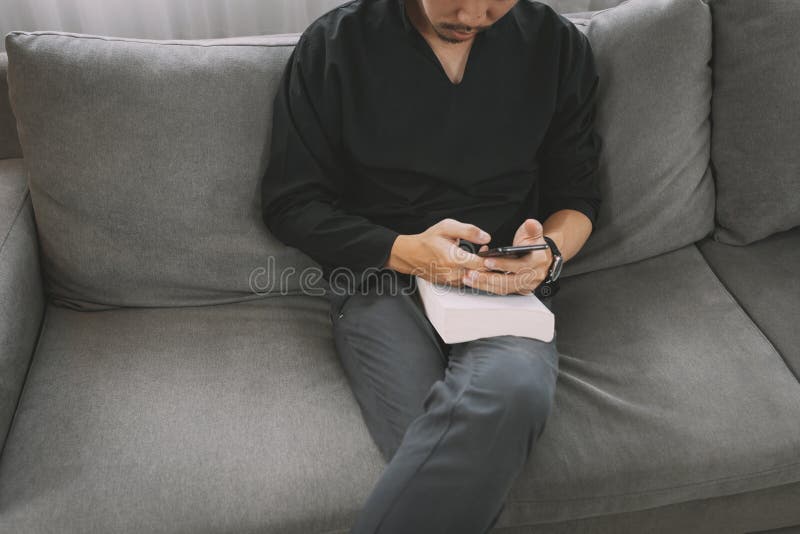 Young Man Sit Down on the Sofa while Using Mobile Phone and Drink ...