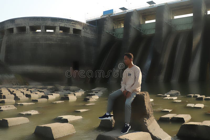 A Young Man Sits on Concrete Blocks Under a Dam Bendungan Sampean Baru ...