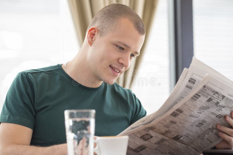 Young Man Sits at a Table, Carefully Reading the Newspaper Ads a Stock ... Young Man Sits at a Table, Carefully Reading the Newspaper Ads a Stock ...