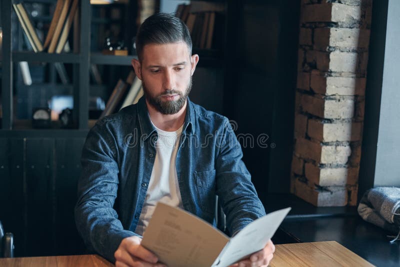Young Man Sitting in a Cafe at the Table and Watching the Menu To Make ...