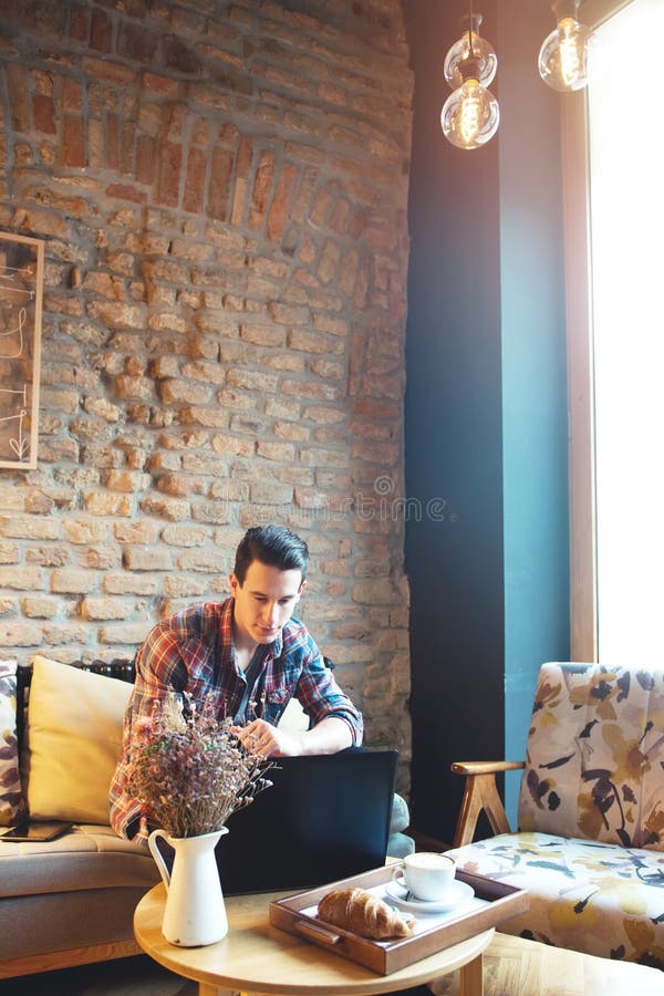 Young Man Sitting at a Cafe, Using a Laptop Stock Photo - Image of ...
