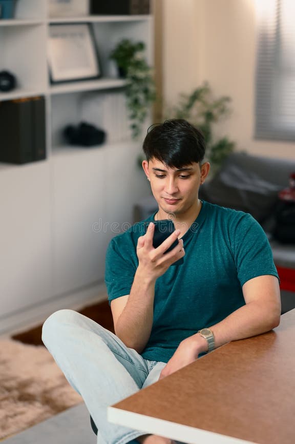 Young Man Sitting Casually at Home, Looking at Smartphone with a ...