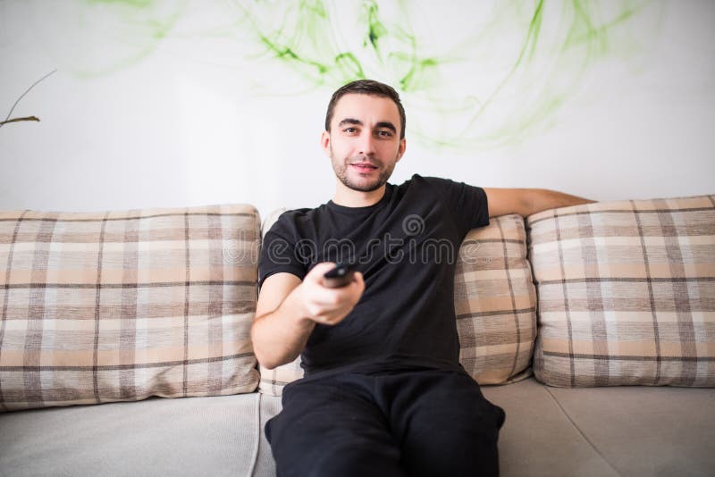 Young Man Sitting on the Couch Using a Remote Control at Home Stock ...