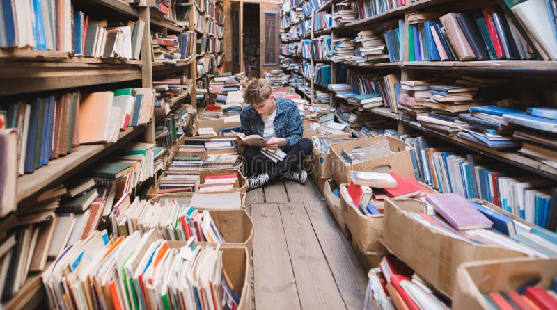 Young Man Sitting on the Floor in an Old Public Library and Reading ...