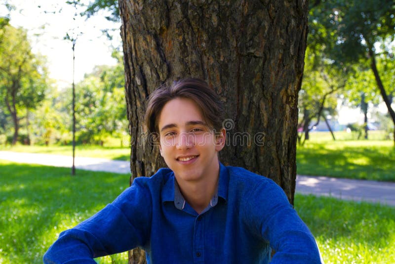 Young Man Sitting at Grass beside Tree at Park, Looking at Camera ...