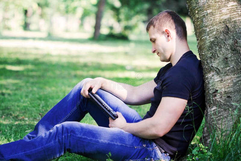 Young Casual Man Sitting on the Ground and Leaning To a Tree Stock ...